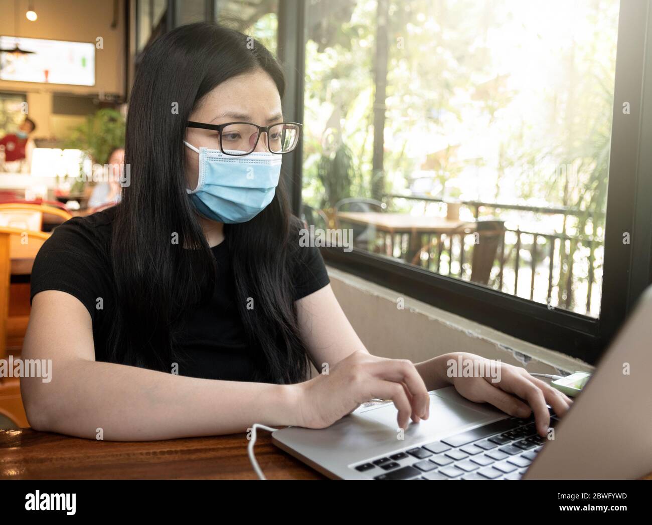 New normal, programmer wearing mask working remotely in cafe during ...