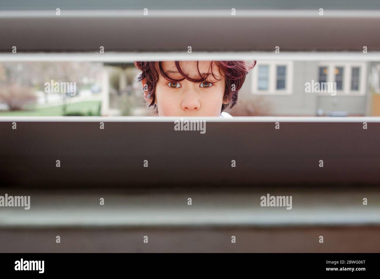 A curious child standing outside peeps into crack of an open window ...