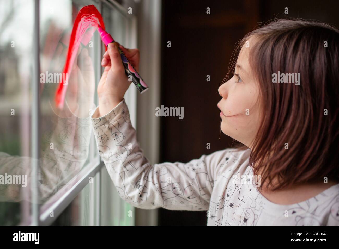 A small serious child draws a rainbow on a window with red marker Stock ...