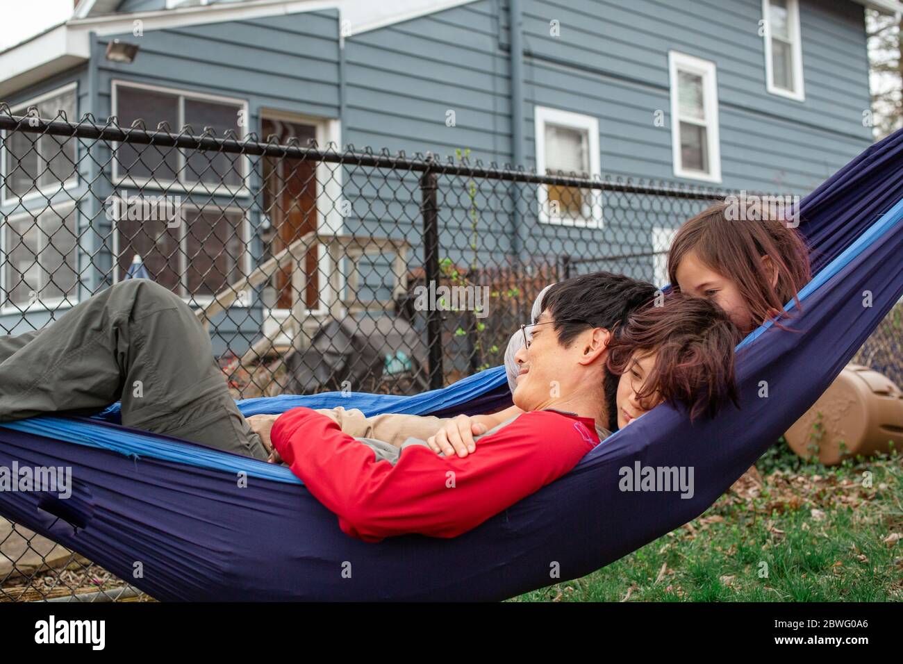Two happy children snuggle their father in a hammock in their backyard ...