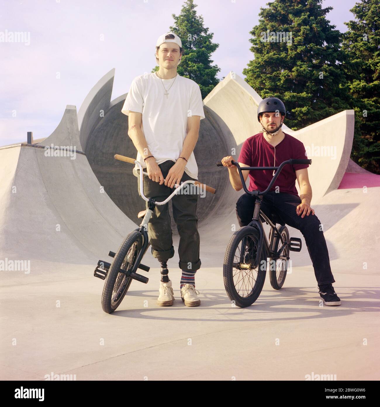 Bmx rider with aputated leg standing with friend in concrete skatepark ...