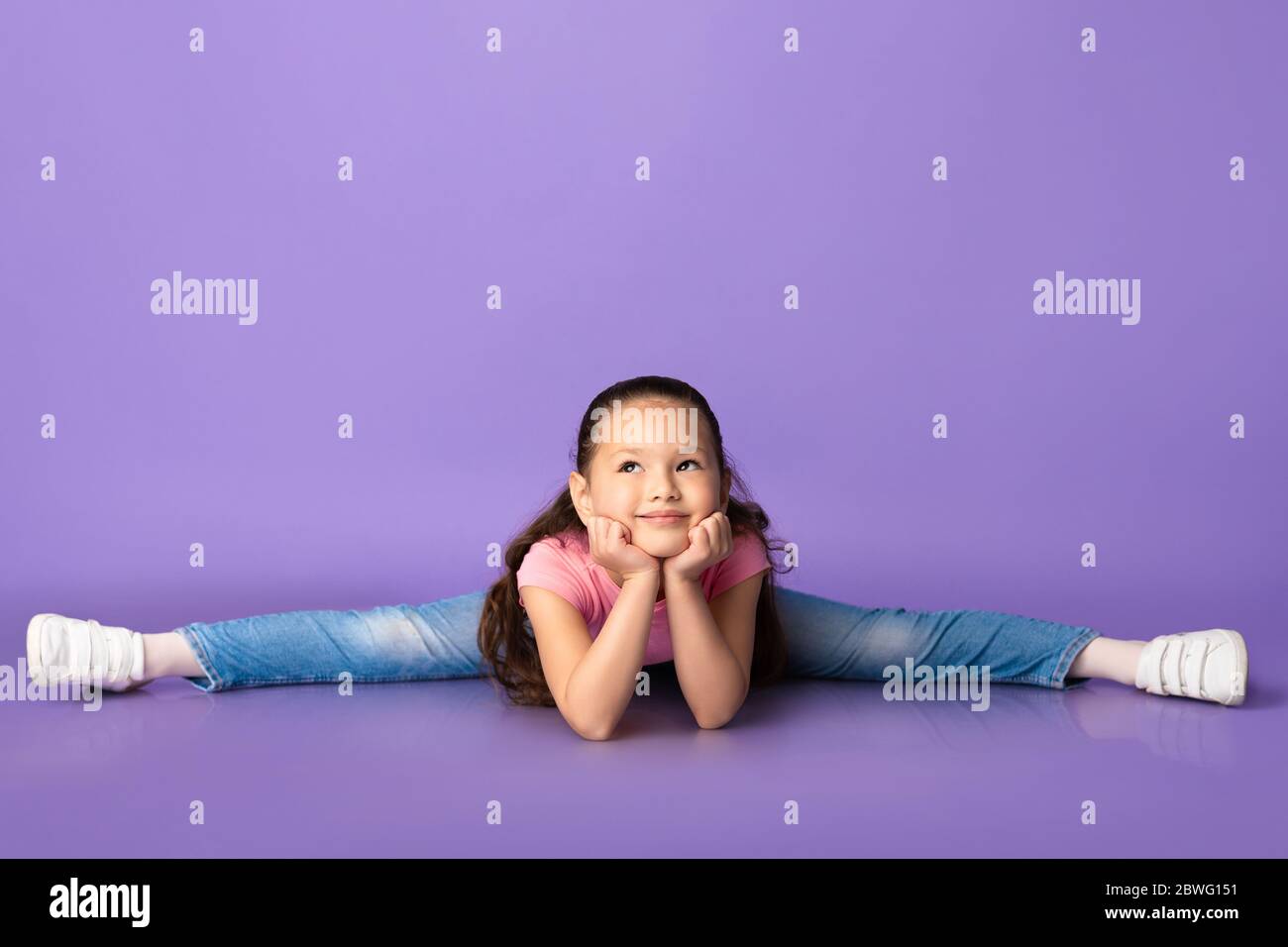 Cute little girl making splits on purple background Stock Photo - Alamy