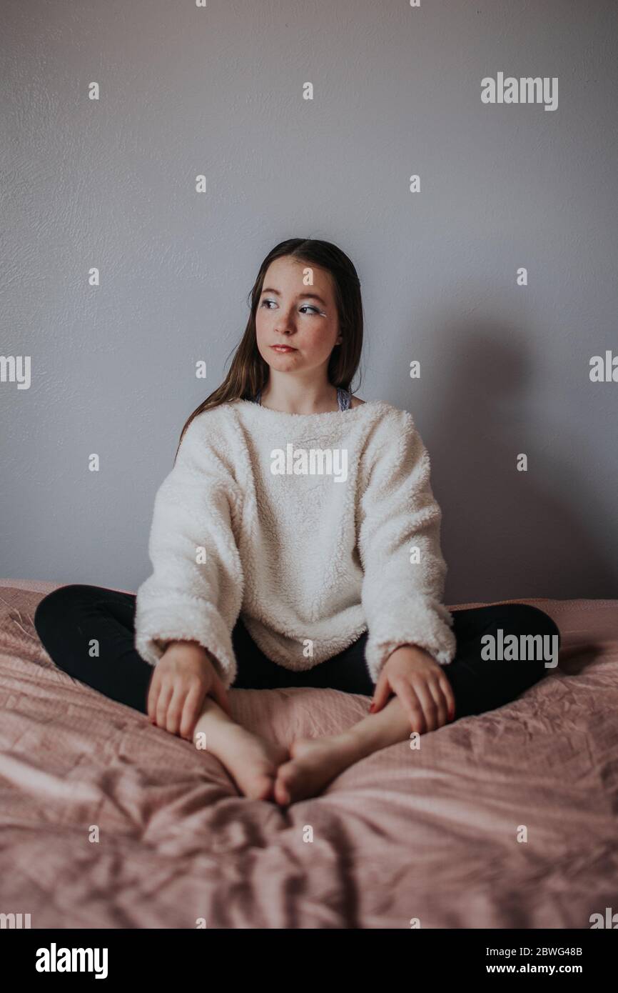 vertical portrait of tween girl sitting on bed looking away Stock Photo ...