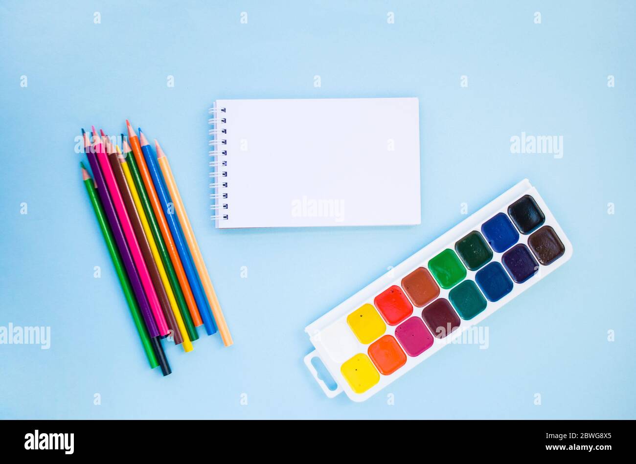 Colorful pencils, notebook, paint brush and watercolors on blue ...