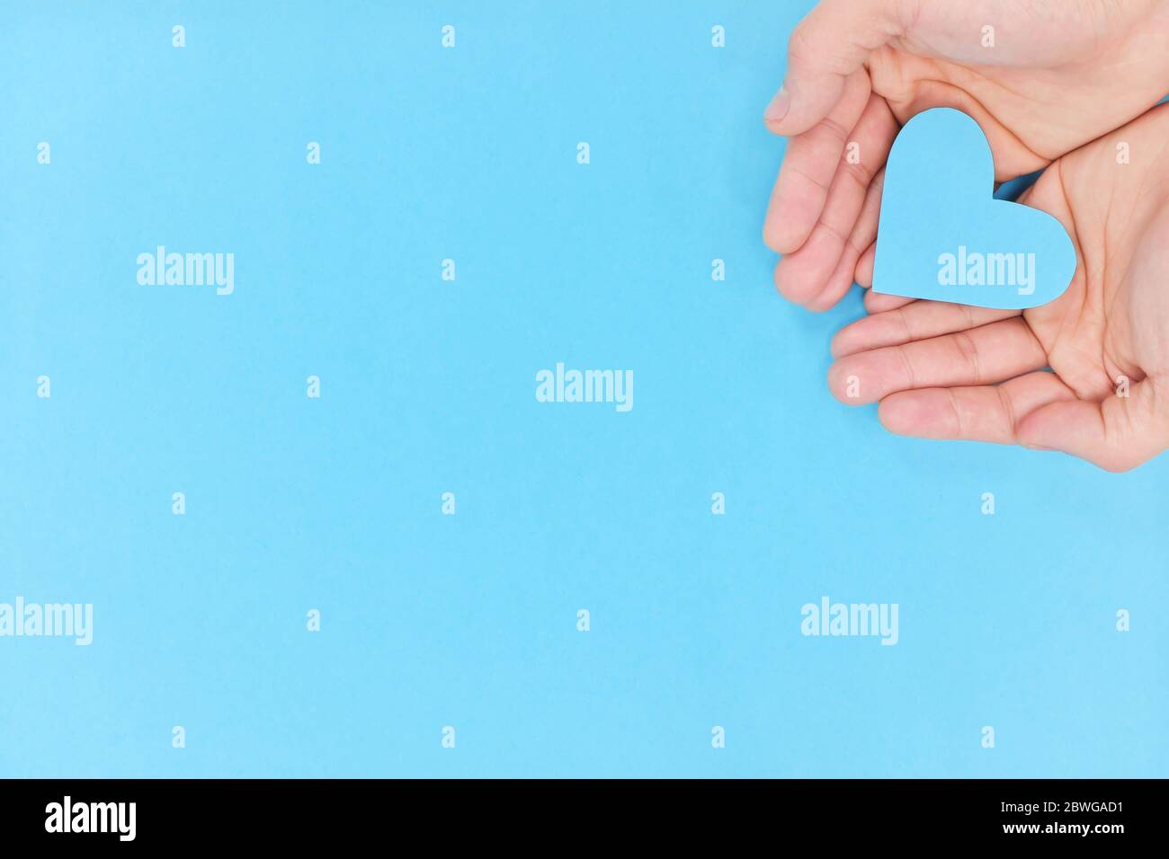 Hands holding a blue heart in blue background. Top view with copy space ...
