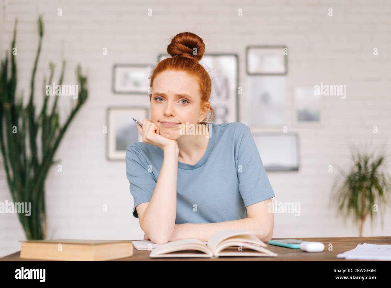 Tired bored girl student sitting at a table with textbooks and a ...