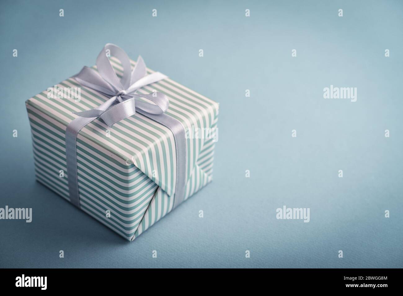 One striped gift box with grey ribbon on blue background closeup Stock ...