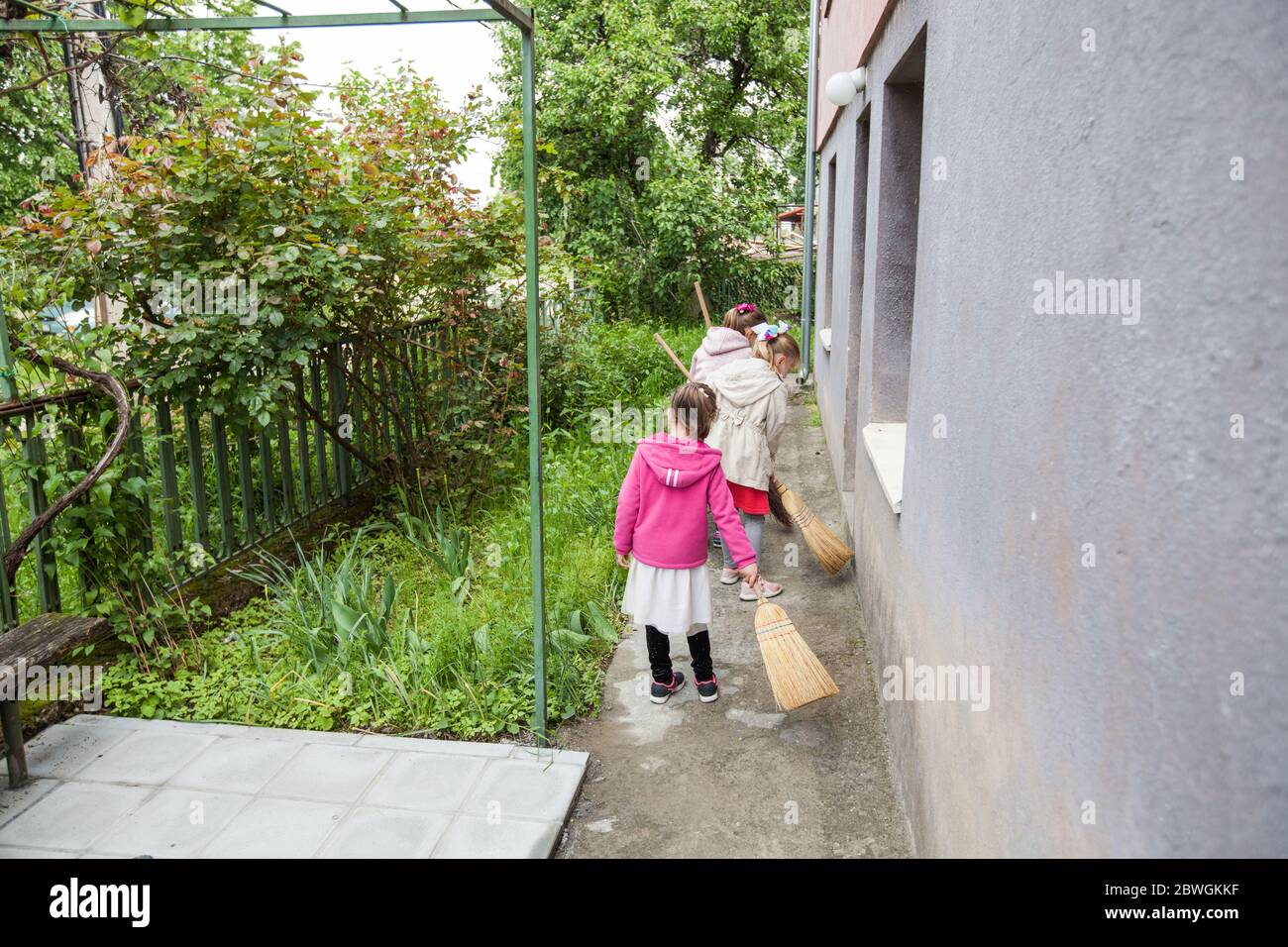 Three little girls cleaning backyard with broom Stock Photo - Alamy