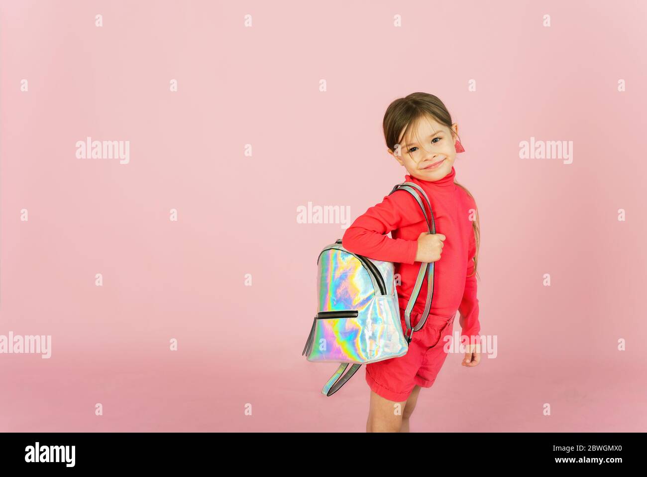 Cute little blonde classmate in a pink suit in the studio with a ...