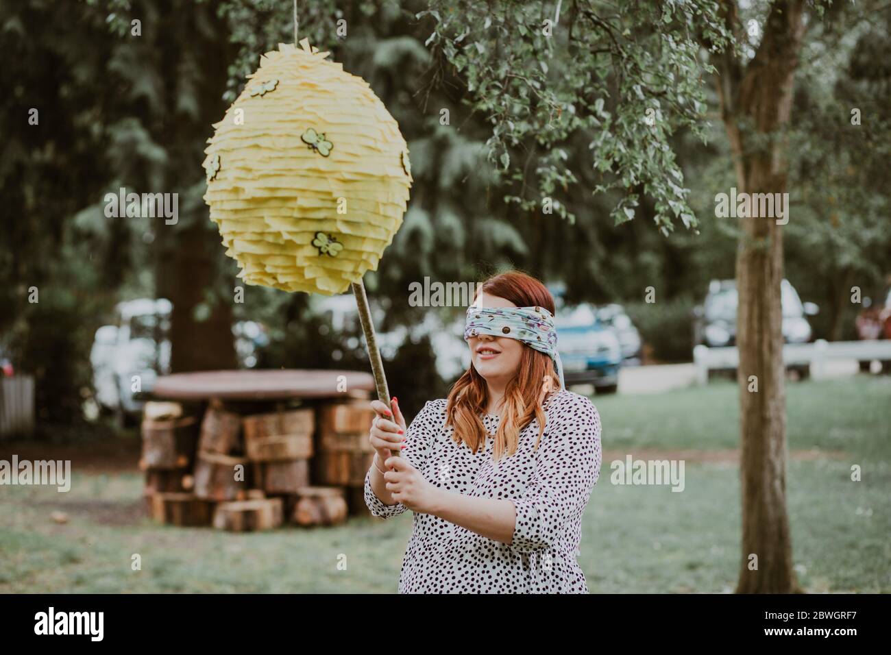 Woman hitting bee hive design pinata wearing blind fold Stock Photo - Alamy