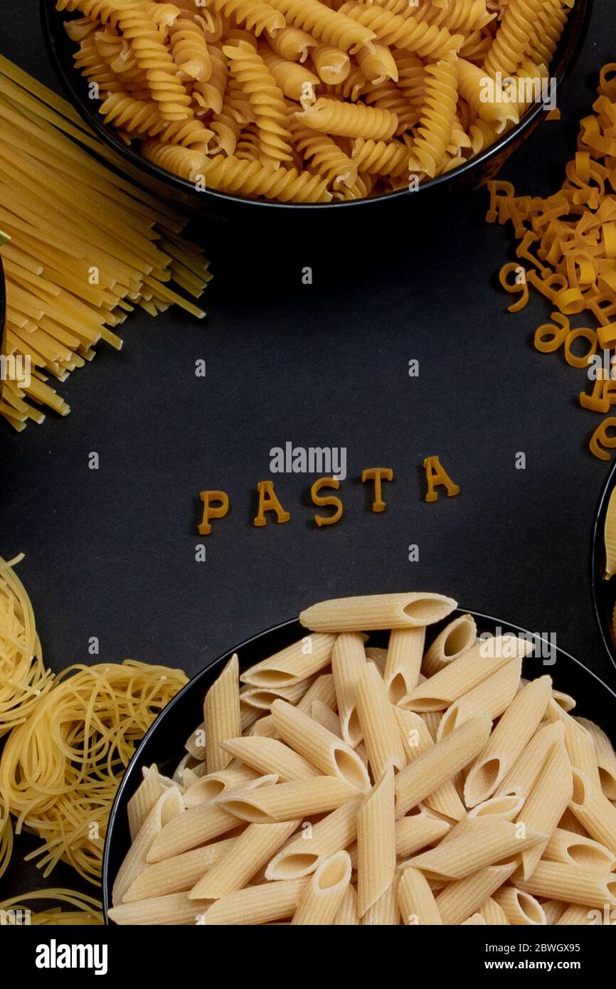 Various mix of pasta on dark background, metal spoons. Food concept ...