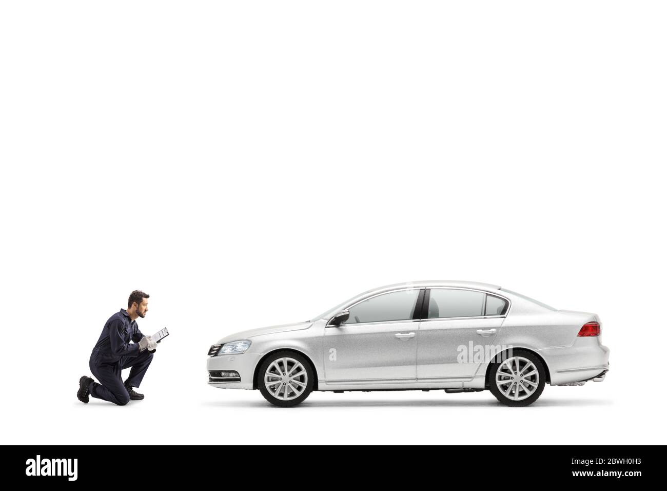 Auto mechanic kneeling in front of a silver car and writing a document ...