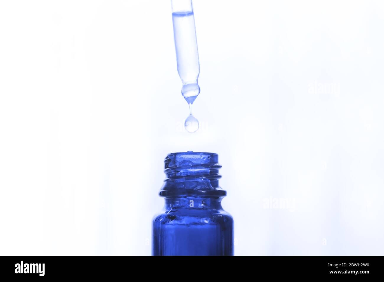 Close up pipette and little drop of acid or serum falling to blue ...