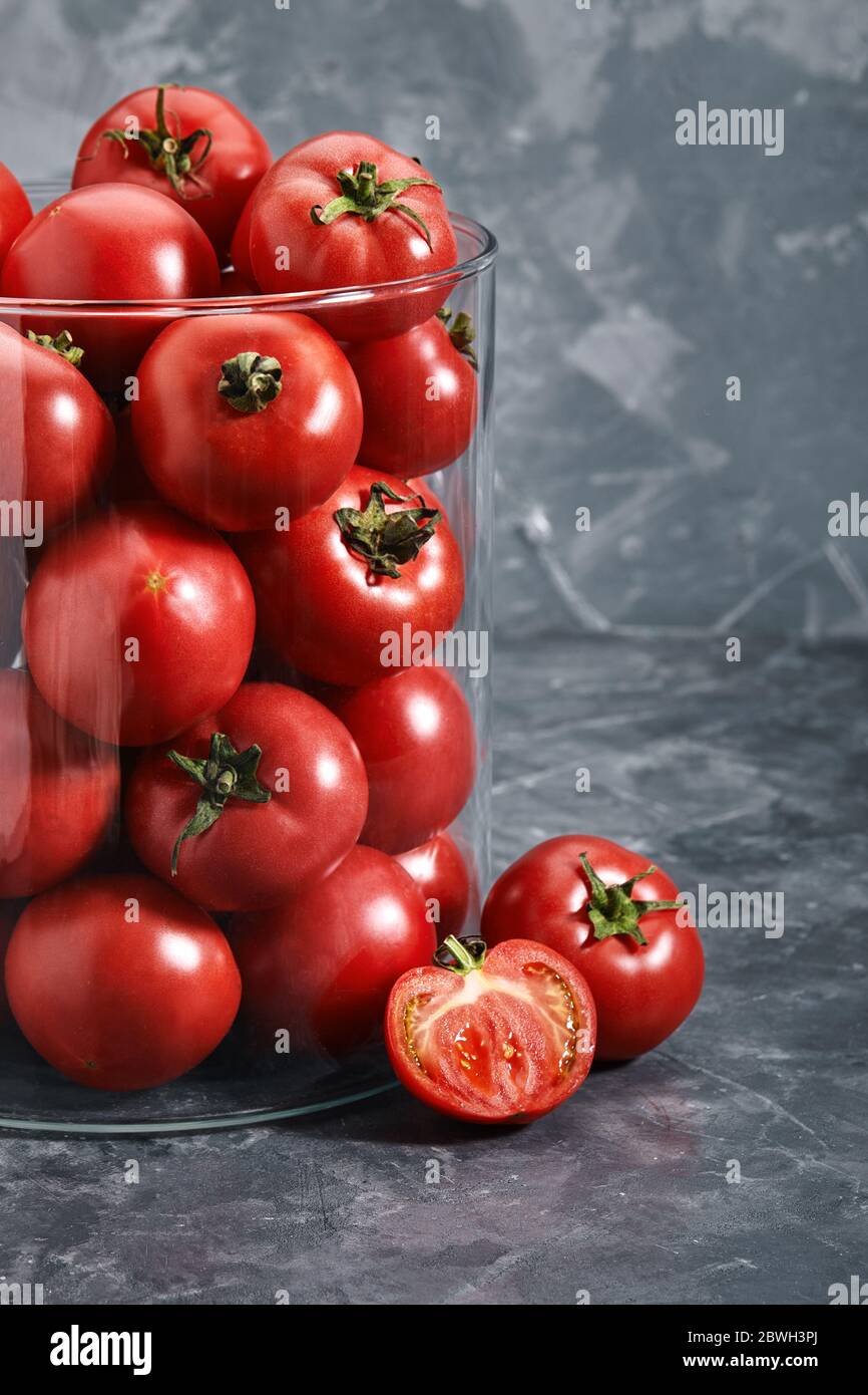 Medium red tomatoes with a glass vase on a gray background. Copy space ...