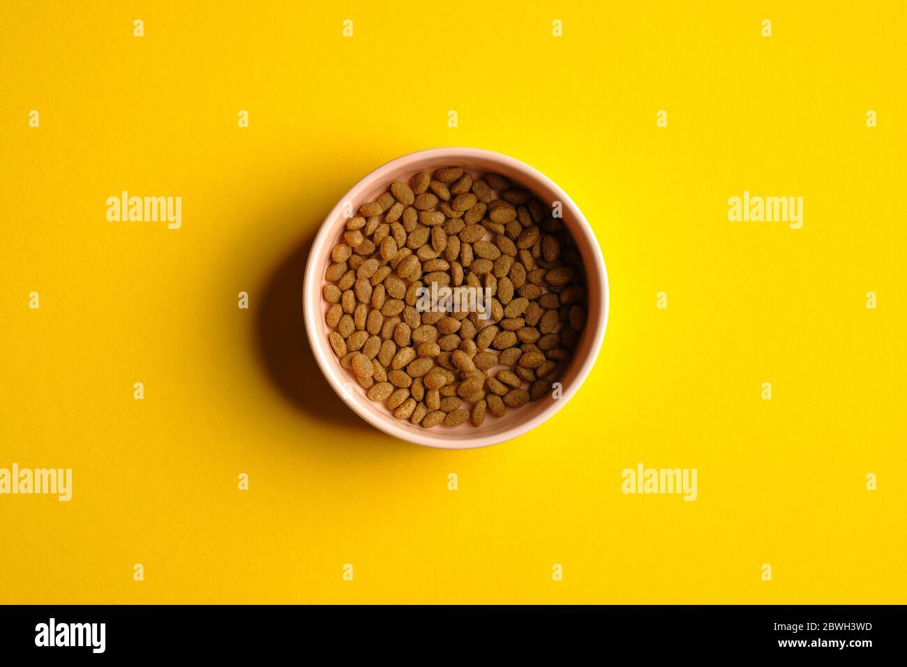 Bowl of dry kibble cat food on yellow background top view. Pet care ...