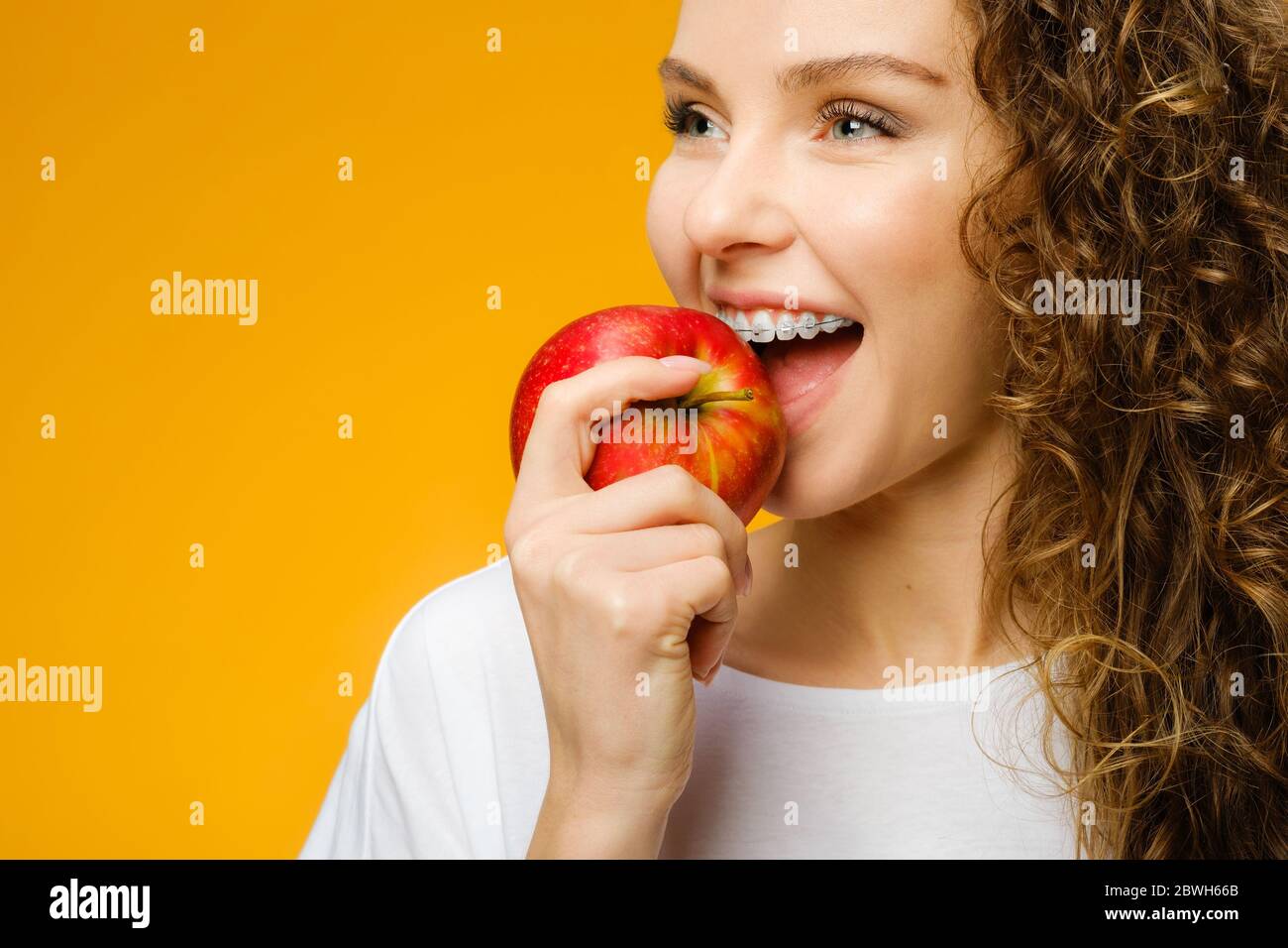 Closeup portrait of pretty caucasian girl with curly hair and red apple ...