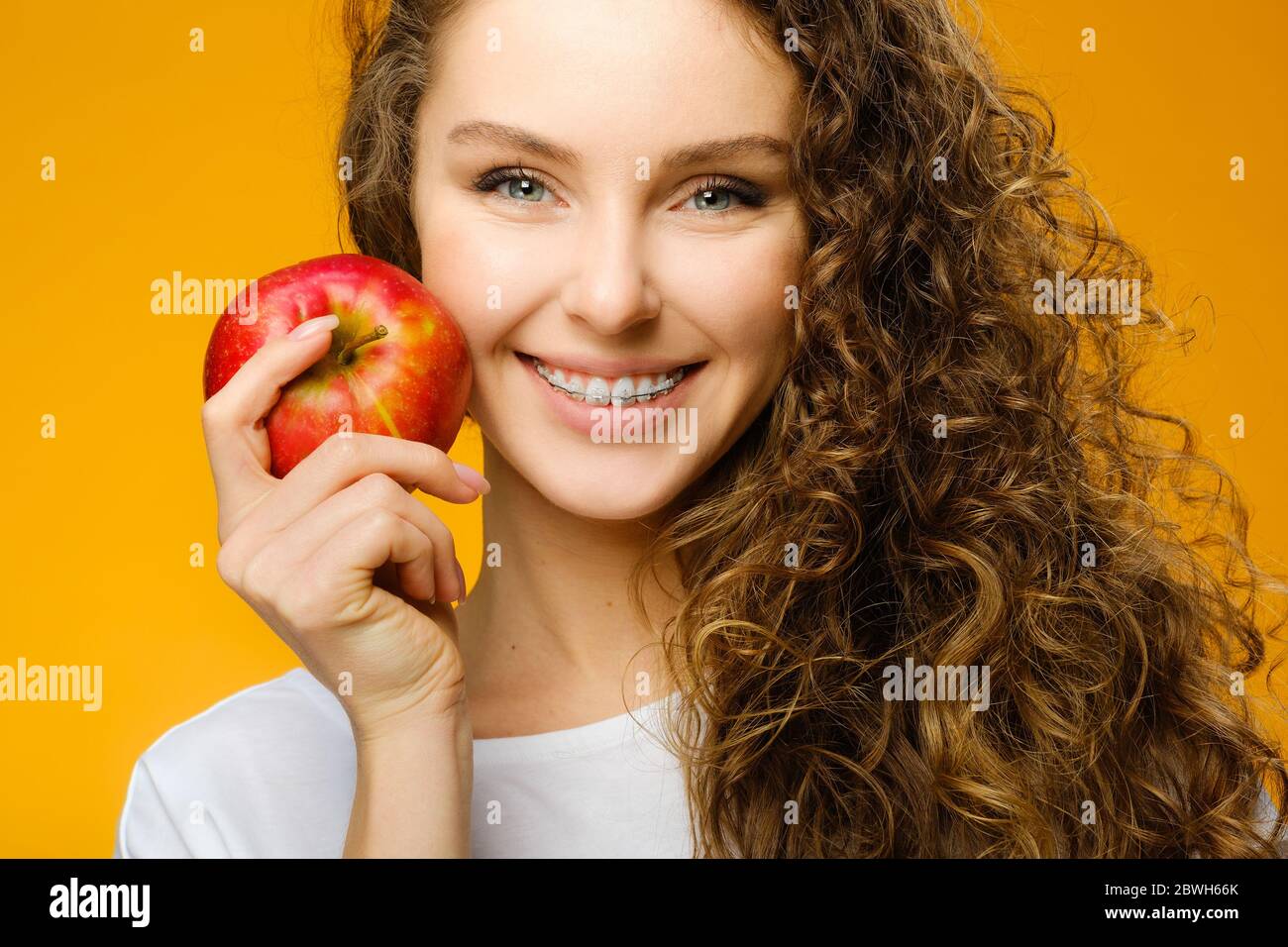 Closeup portrait of pretty caucasian girl with curly hair and red apple ...