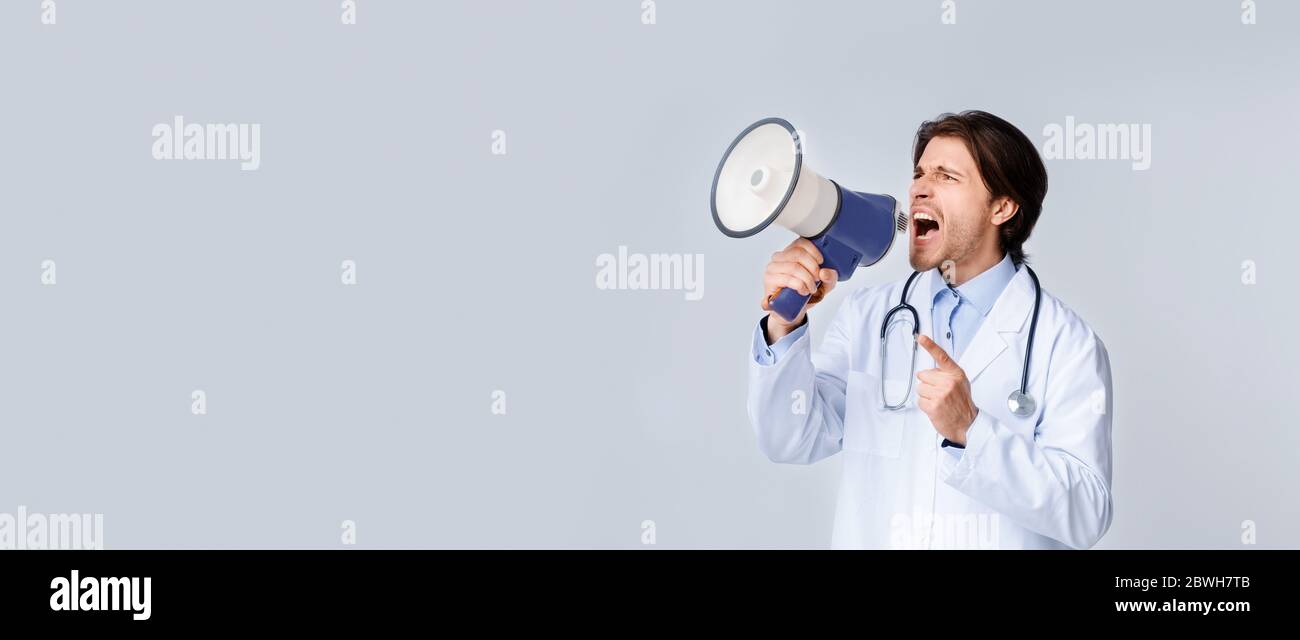 Angry male doctor shouting with megaphone at copy space on light ...