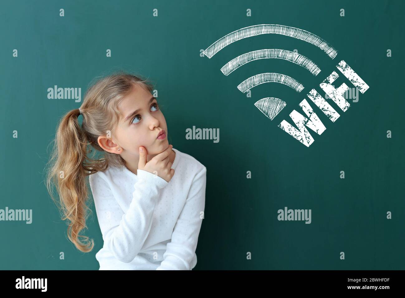 Thoughtful little schoolgirl near blackboard with drawn wifi symbol in ...