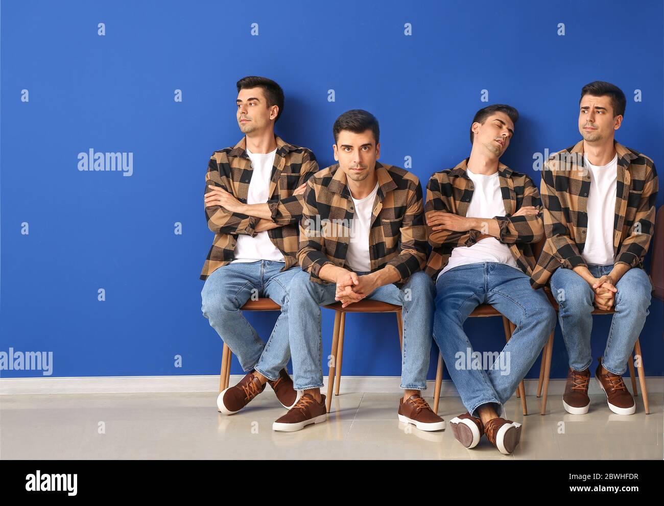 Waiting young men sitting on chairs near color wall Stock Photo - Alamy