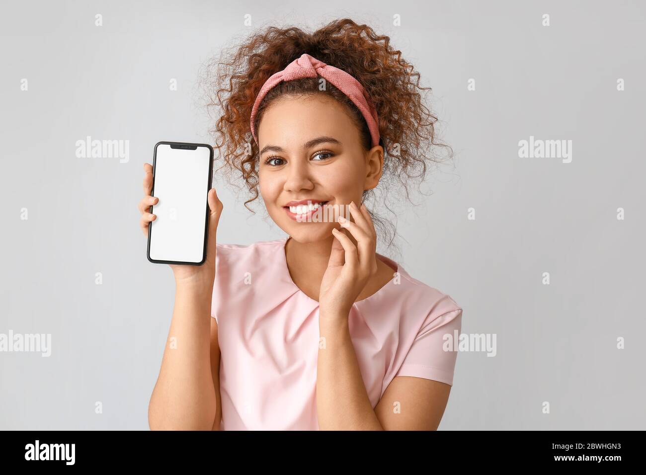 Beautiful young African-American woman with mobile phone on grey ...