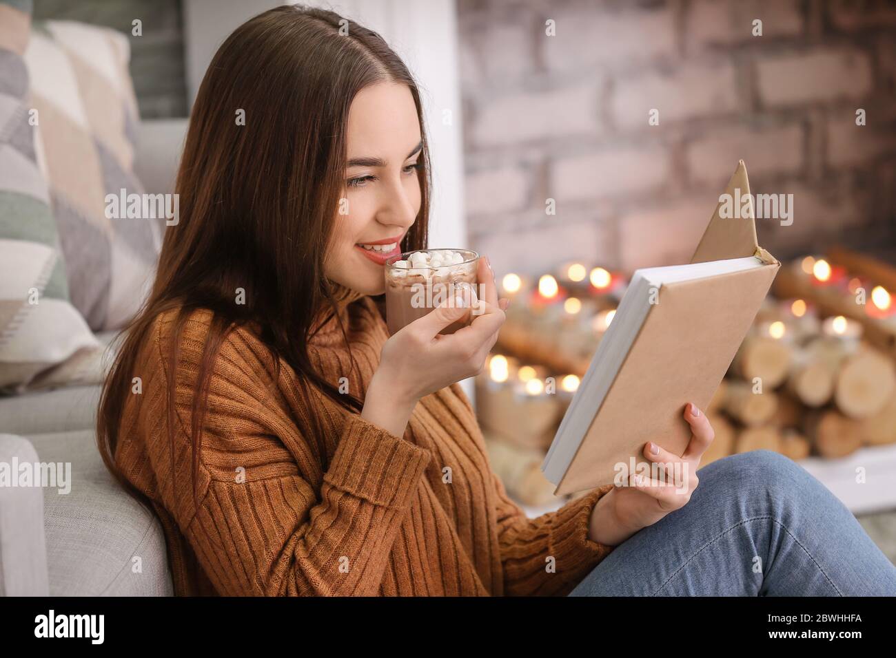 Beautiful young woman drinking hot cocoa and reading book at home Stock ...