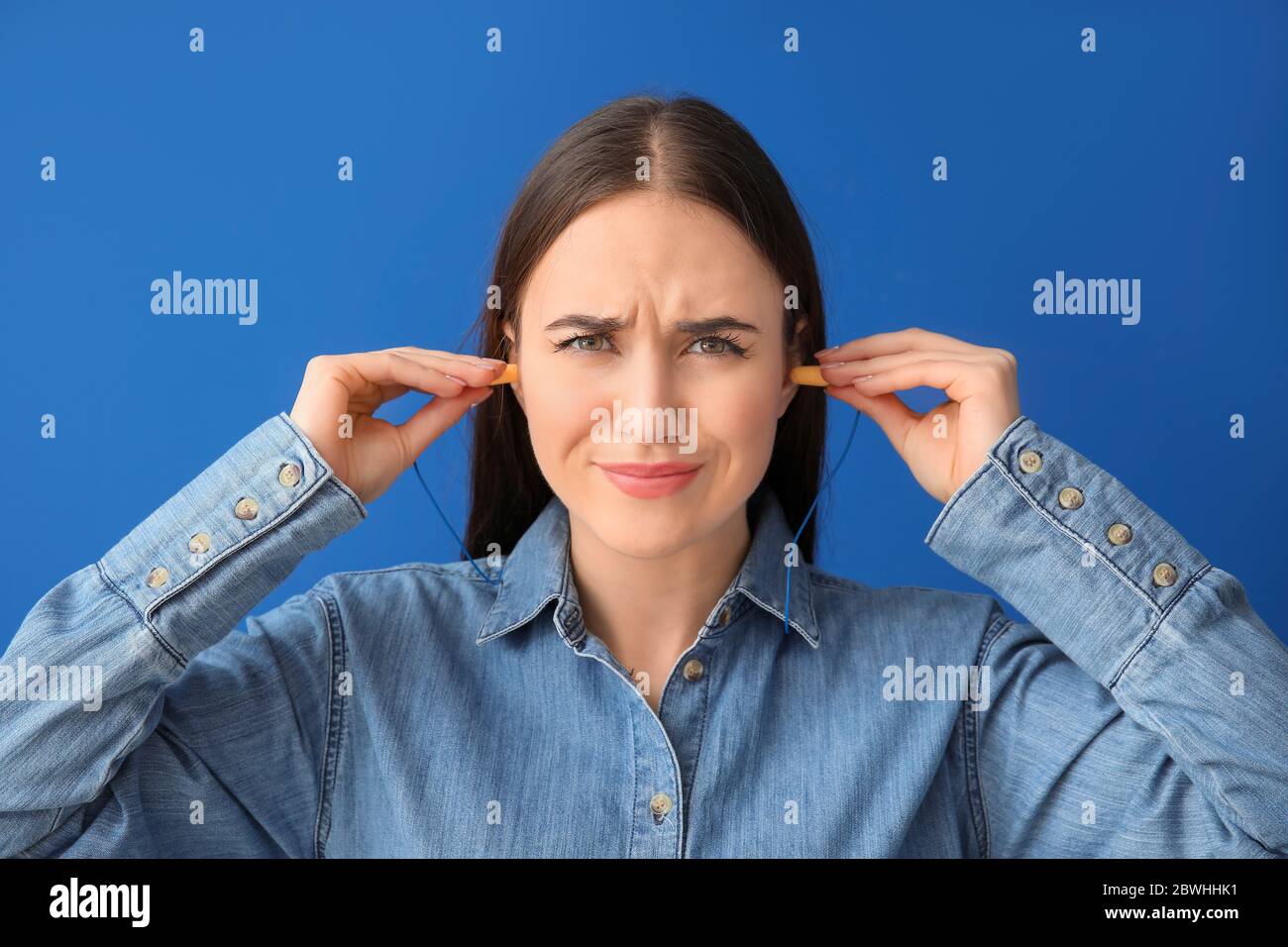 Young woman with ear plugs suffering from loud noise on color ...