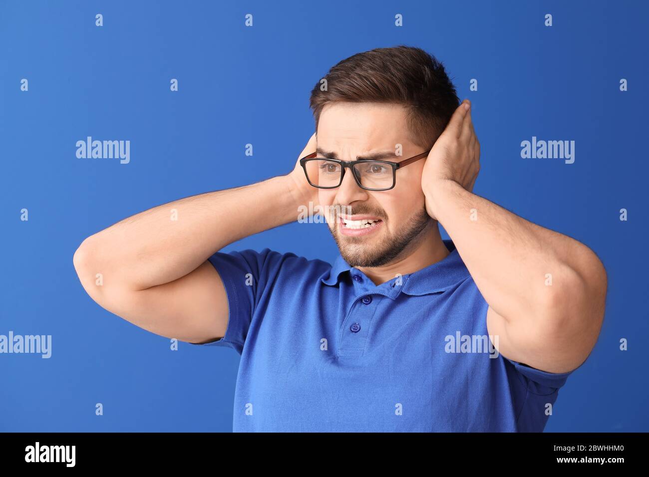 Young man suffering from loud noise on color background Stock Photo - Alamy
