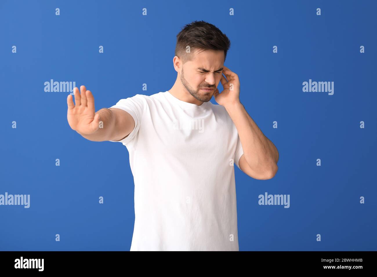 Young man suffering from loud noise on color background Stock Photo - Alamy