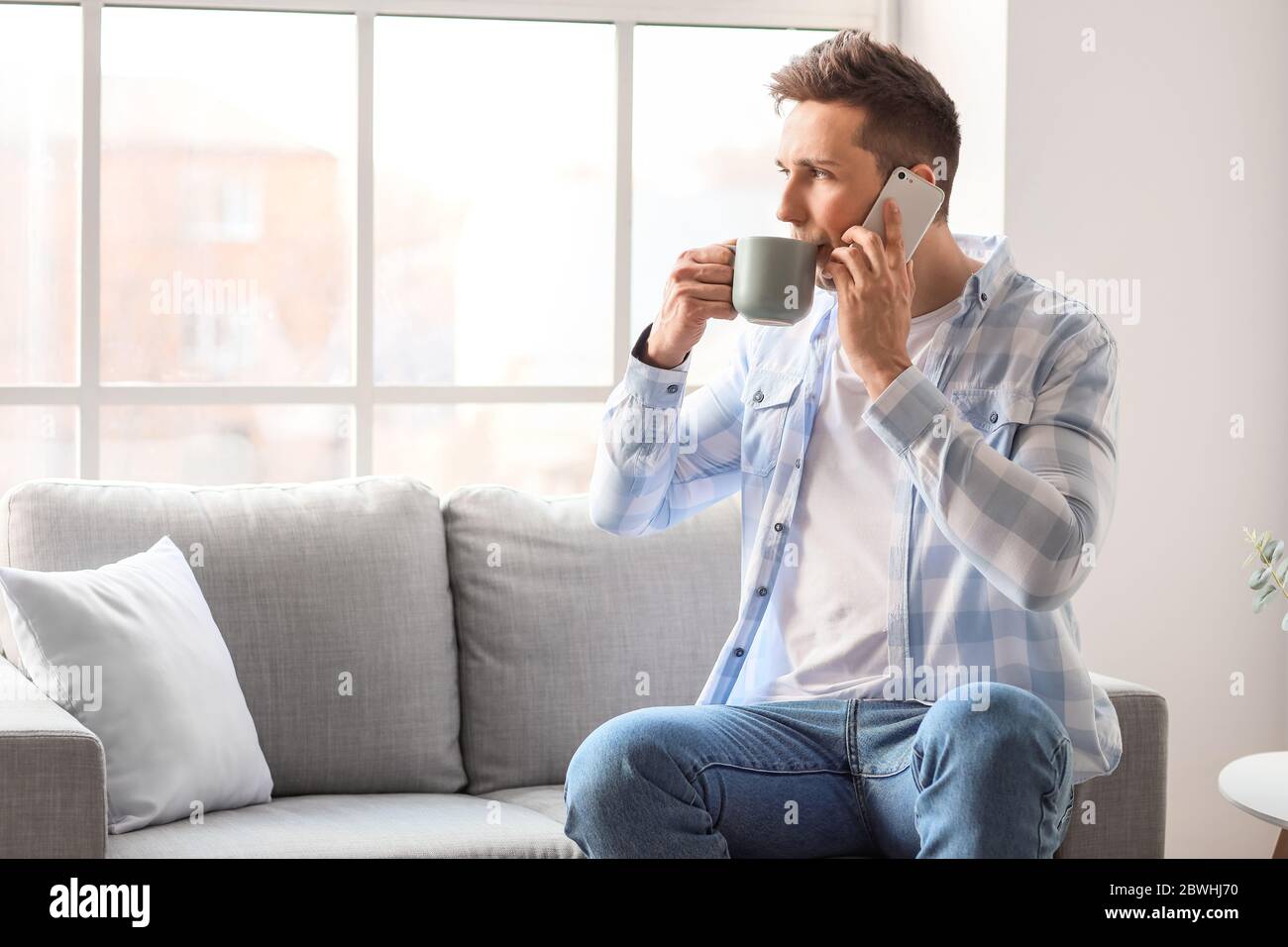 Handsome man drinking coffee while talking by phone at home Stock Photo ...