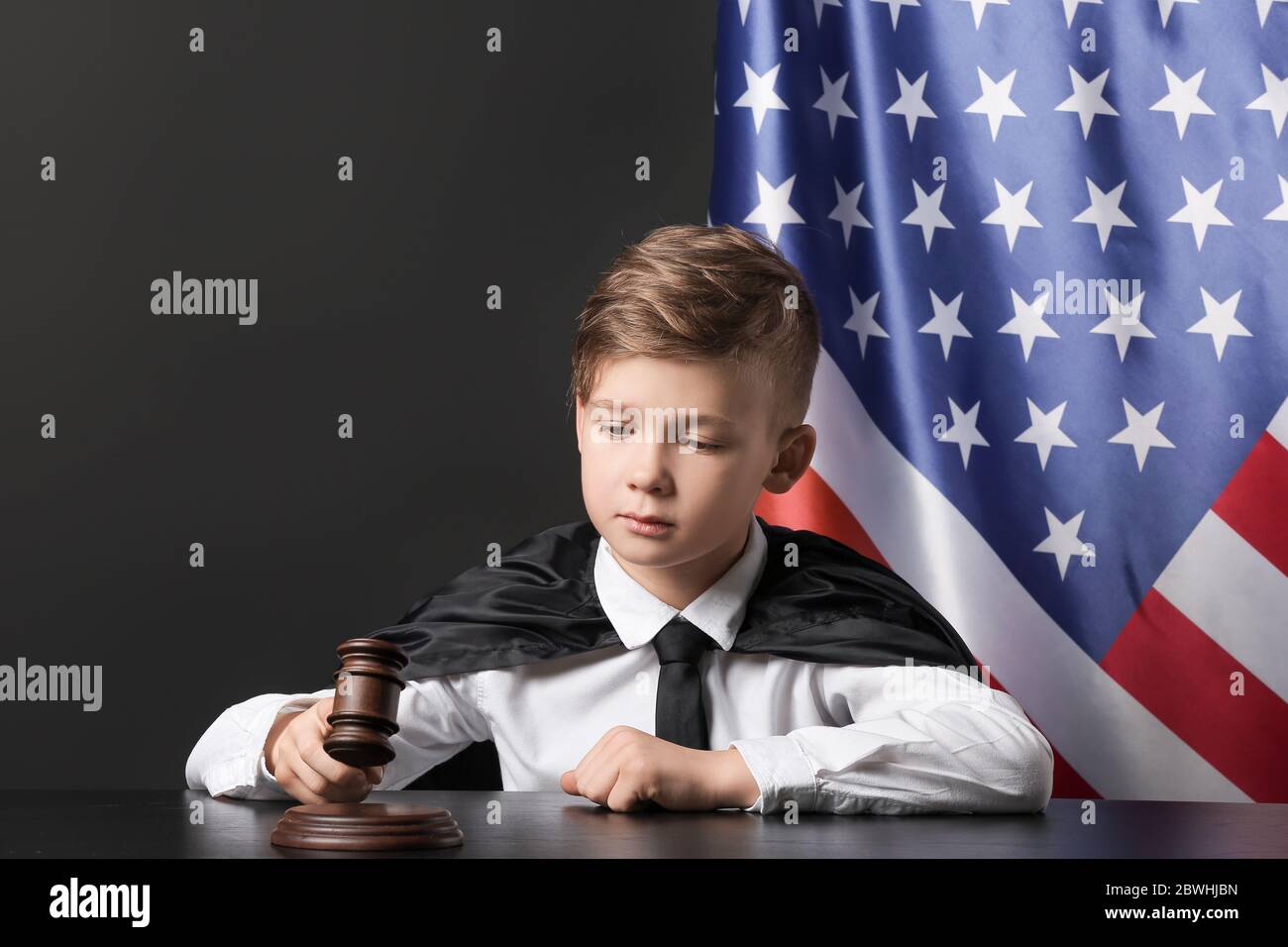 Little judge sitting at table near national flag of USA on dark ...