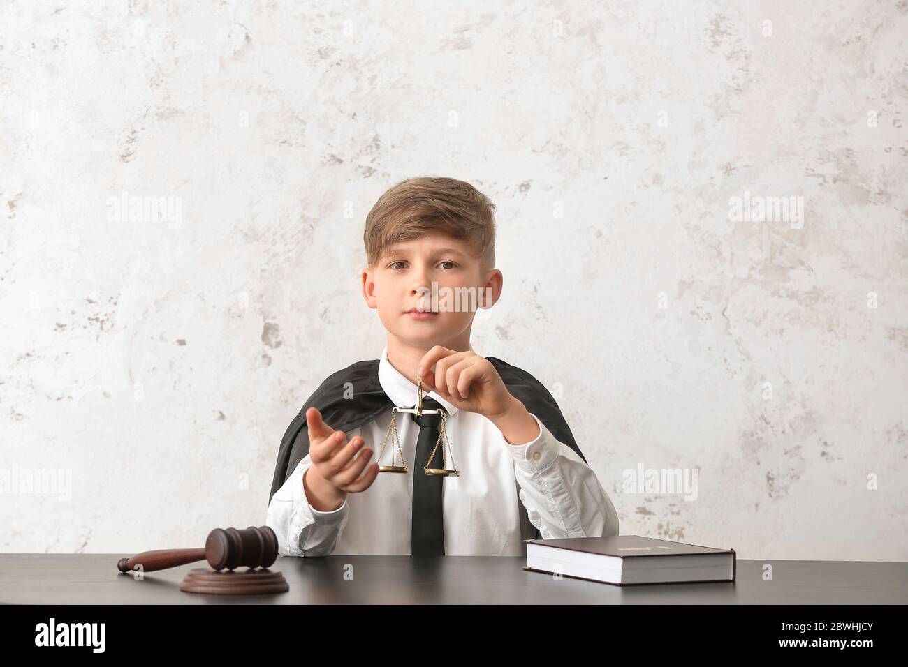 Portrait of little judge sitting at table against white background ...