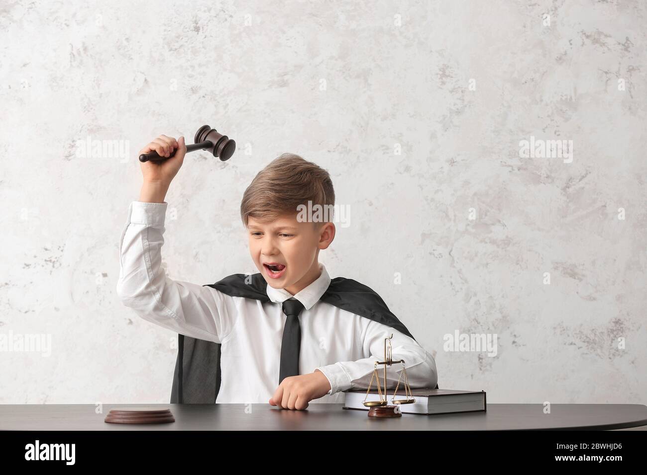 Portrait of little judge sitting at table against white background ...
