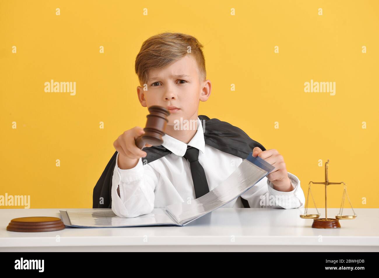 Portrait of little judge sitting at table against color background ...