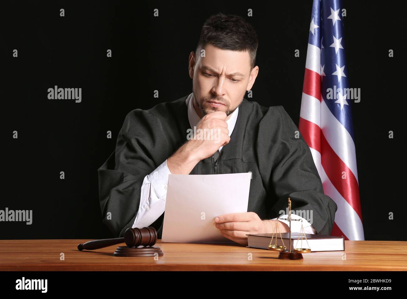 Male judge reading documents at table on dark background Stock Photo ...
