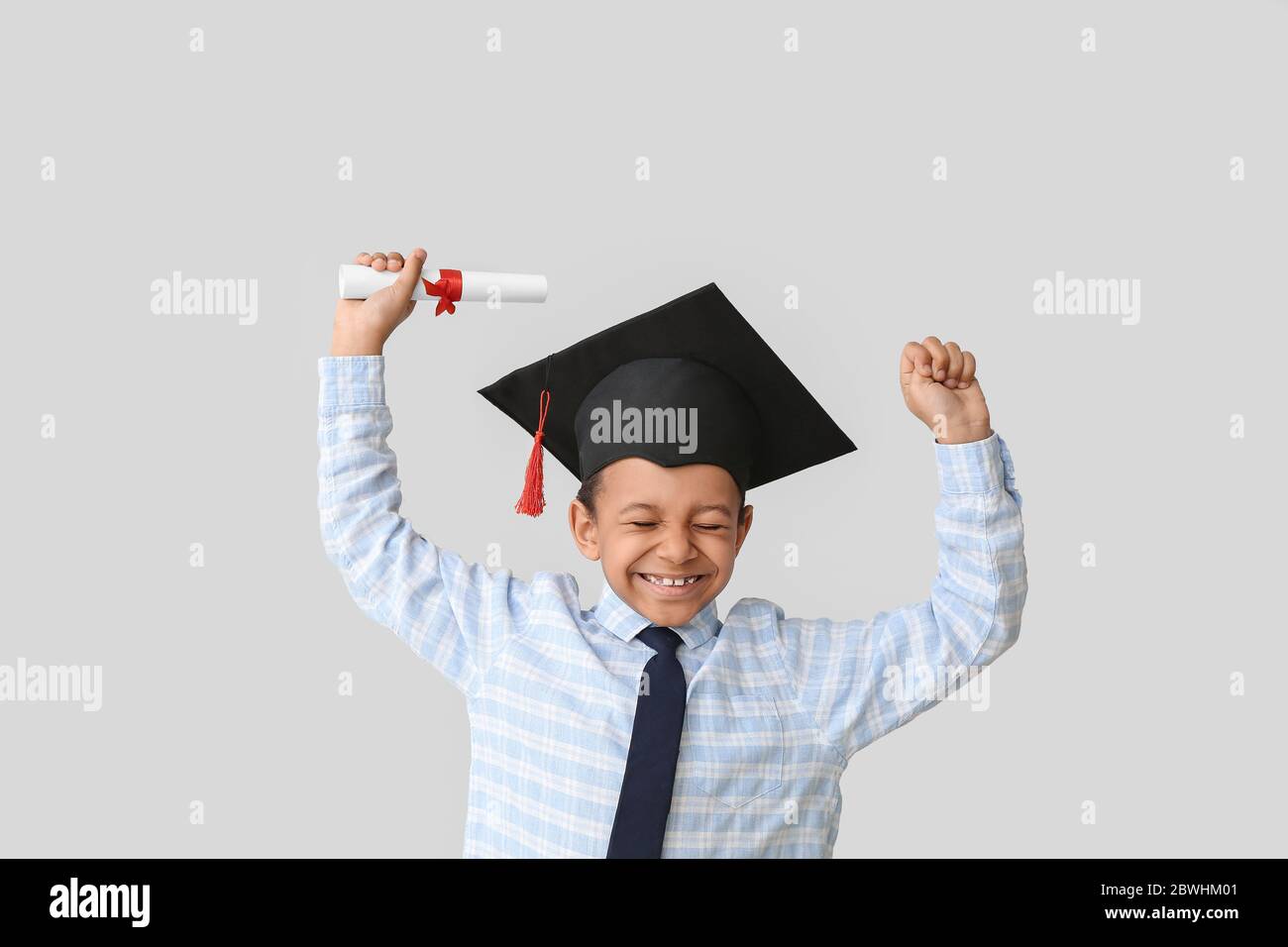 Happy African-American boy in graduation hat and with diploma on grey ...