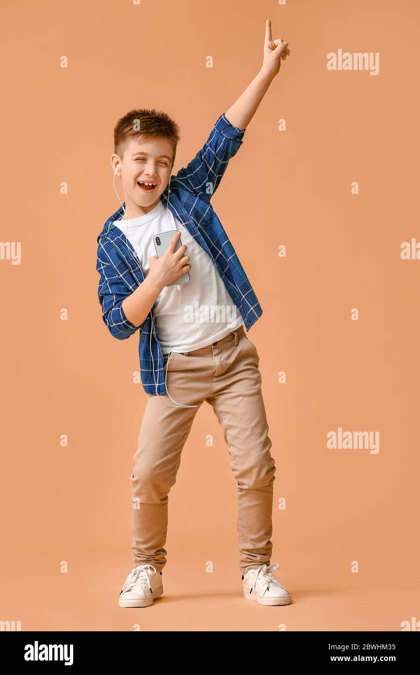Cute little boy dancing and listening to music against color background ...