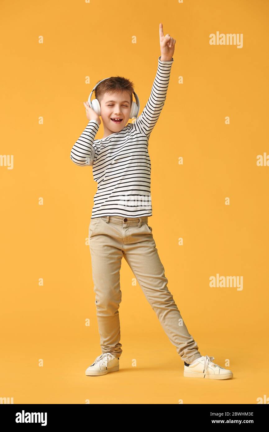 Cute little boy dancing and listening to music against color background ...
