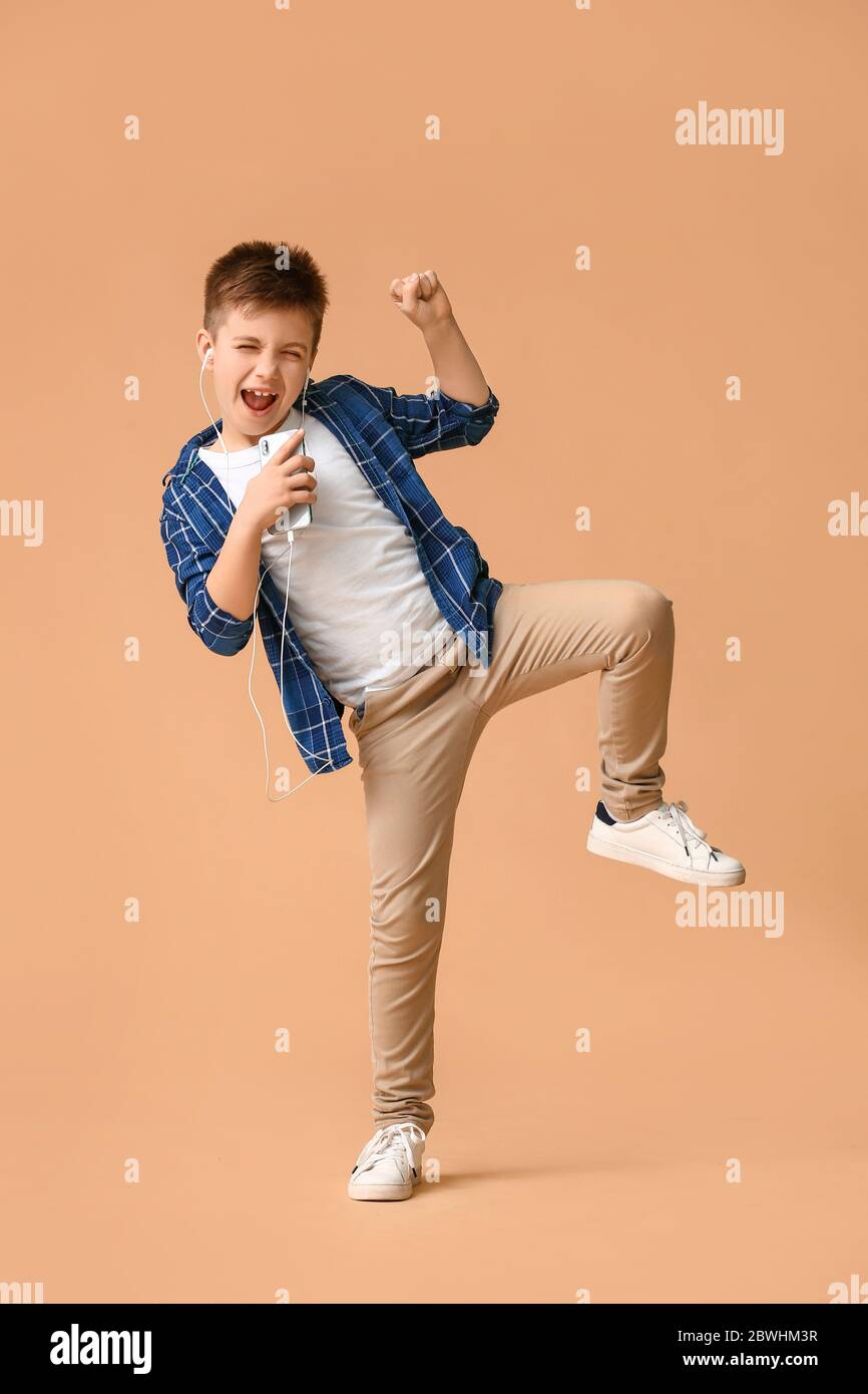 Cute little boy dancing and listening to music against color background ...