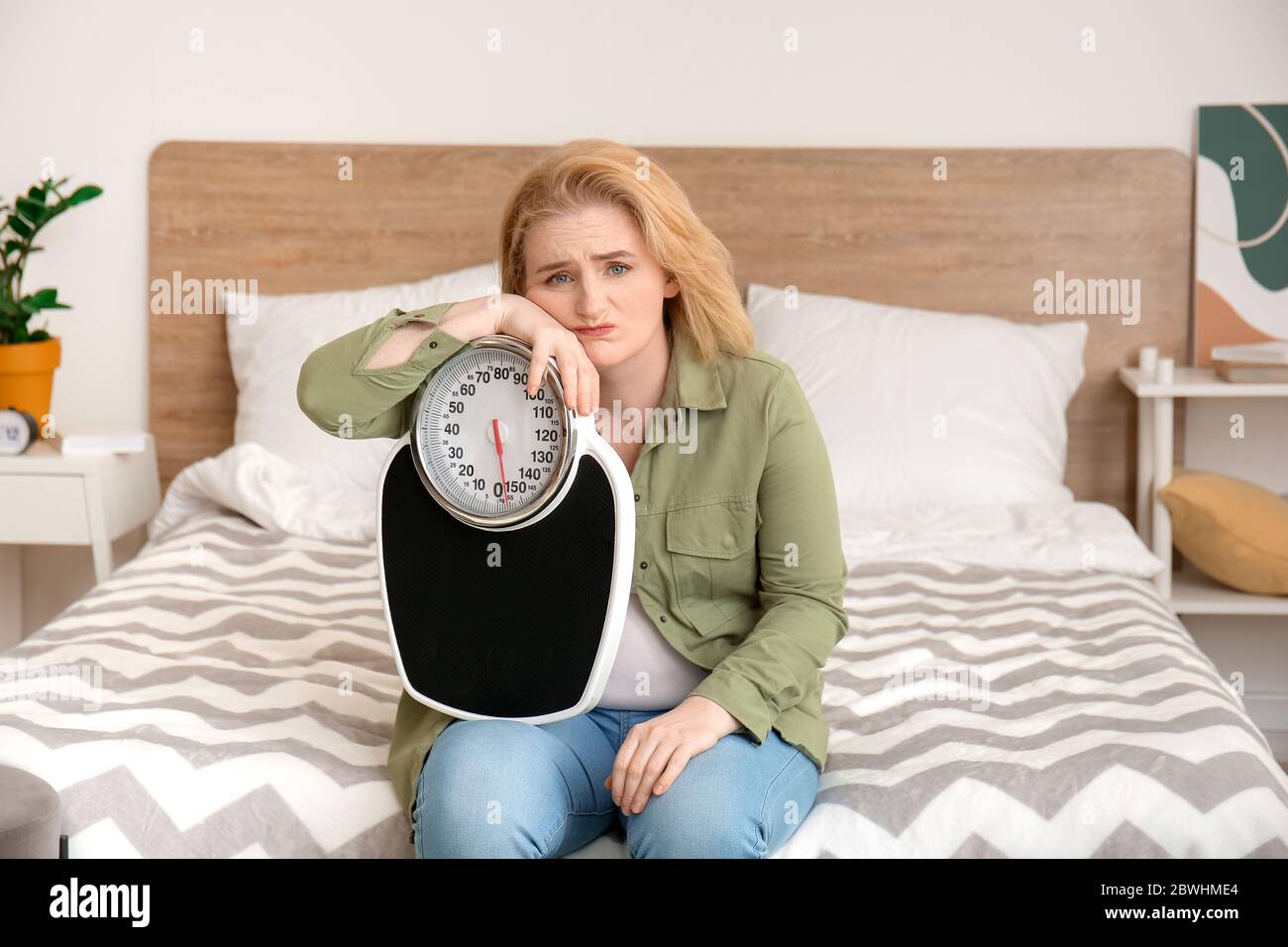 Sad overweight woman with scales at home Stock Photo - Alamy