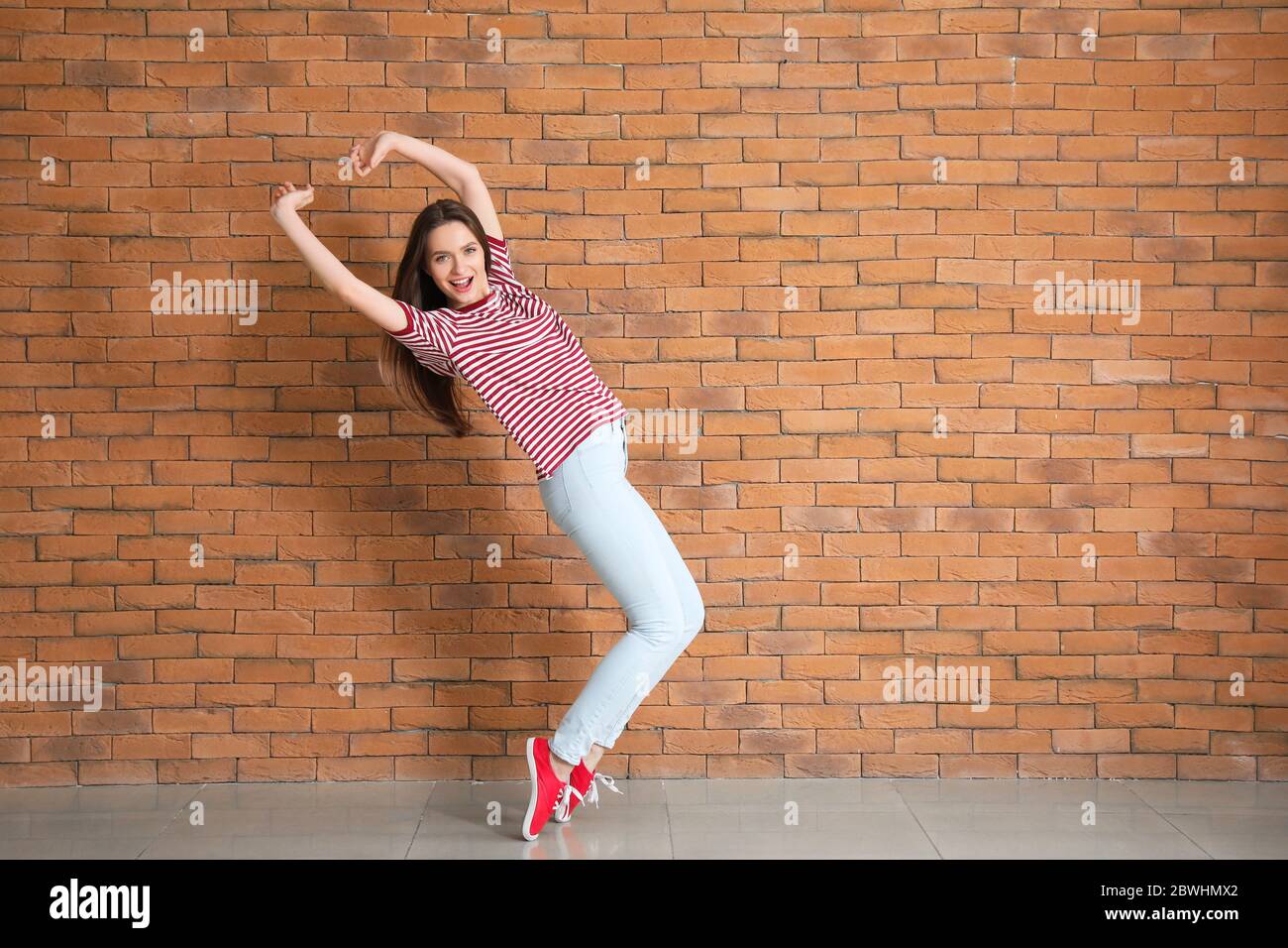 Beautiful young woman dancing near brick wall Stock Photo - Alamy
