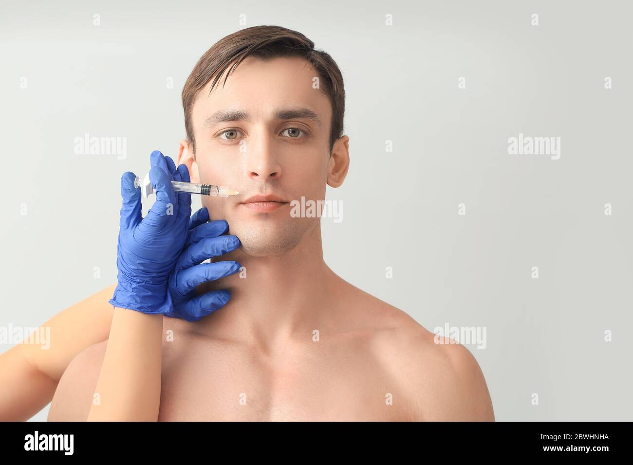 Handsome man receiving filler injection on light background Stock Photo ...