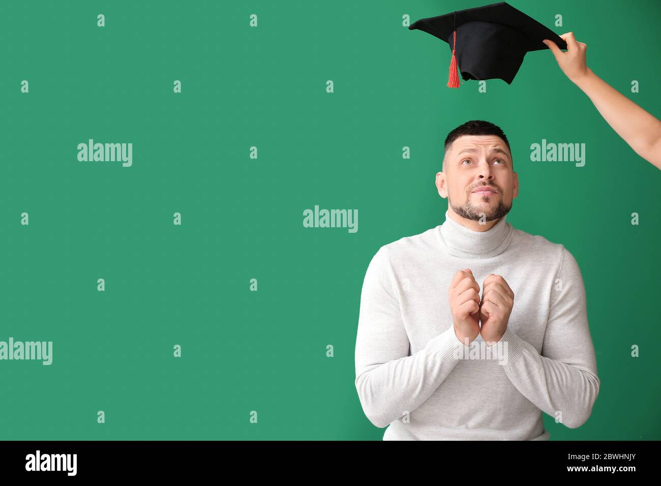 Hand putting graduation hat on man's head against color background ...