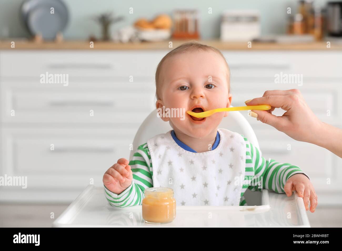 Mother feeding cute baby in kitchen Stock Photo - Alamy