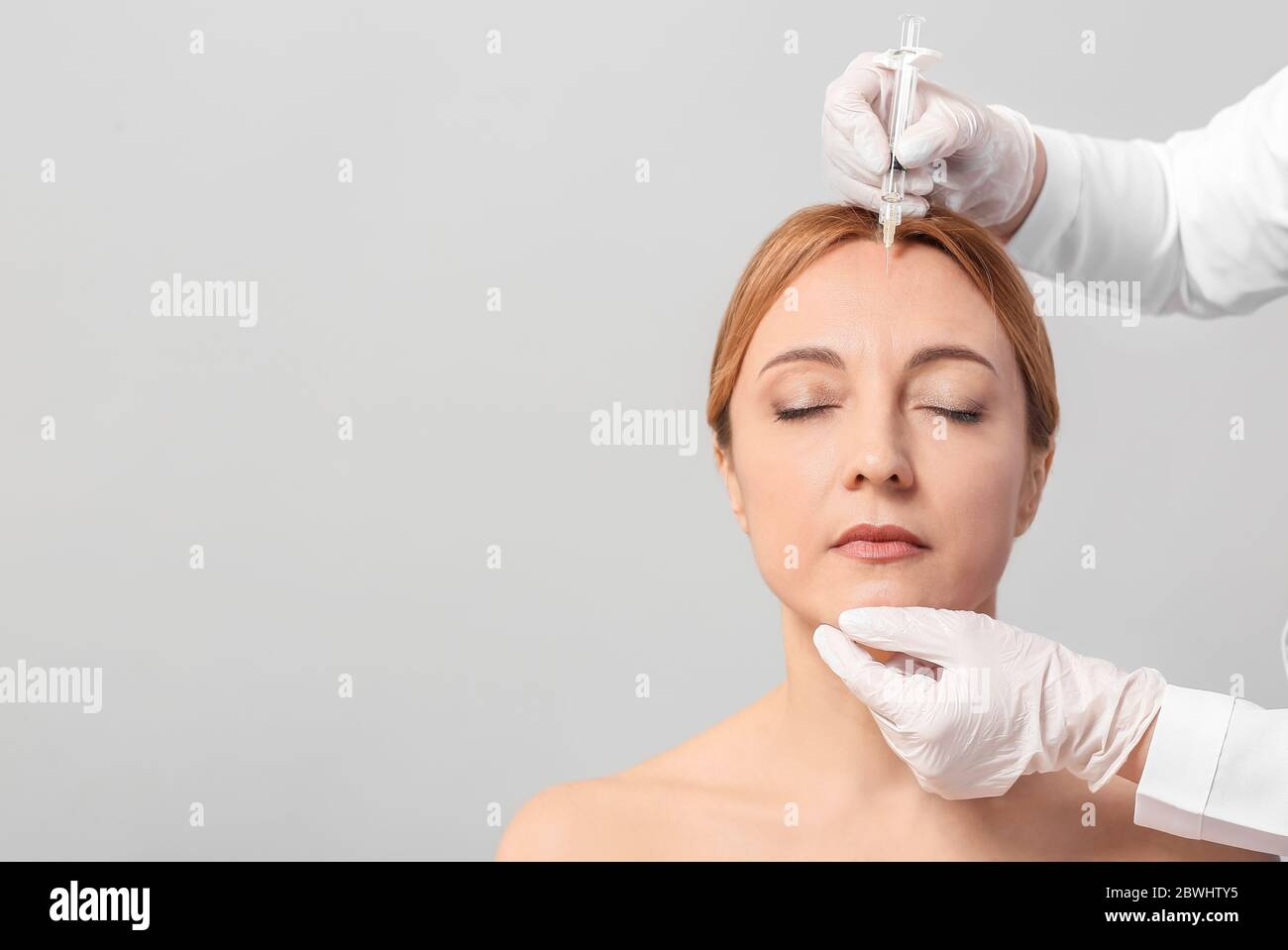 Woman receiving filler injection against grey background Stock Photo ...