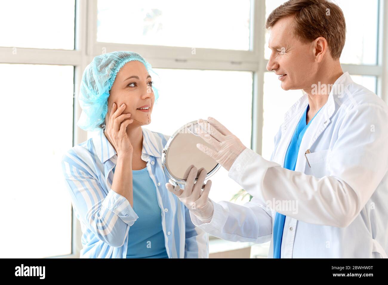 Plastic surgeon showing woman her reflection in mirror Stock Photo - Alamy