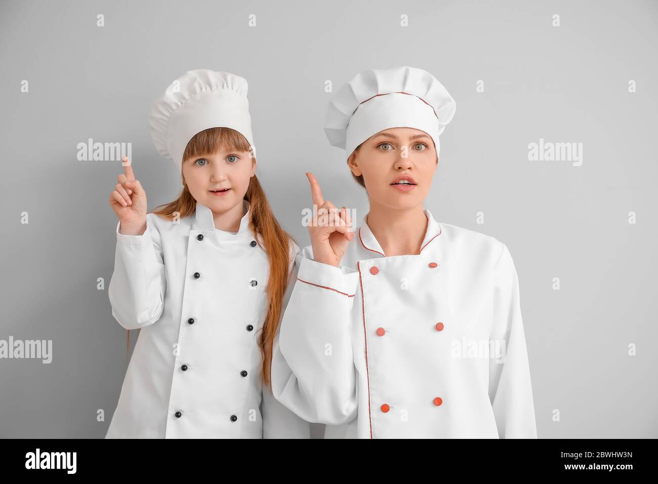 Portrait of female chef and her little daughter with raised index ...