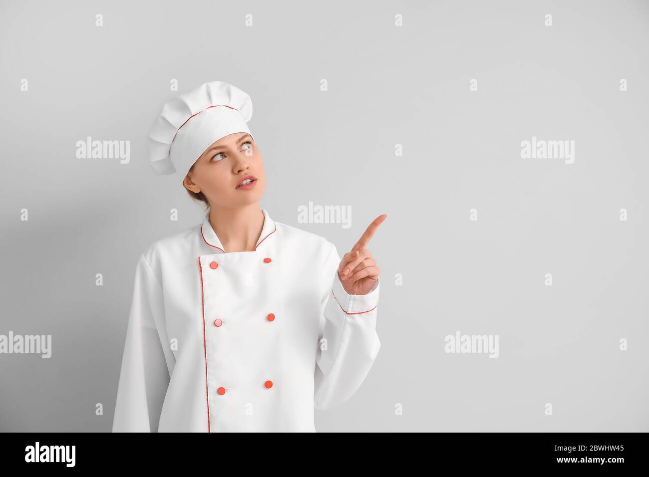Beautiful female chef pointing at something on light background Stock ...