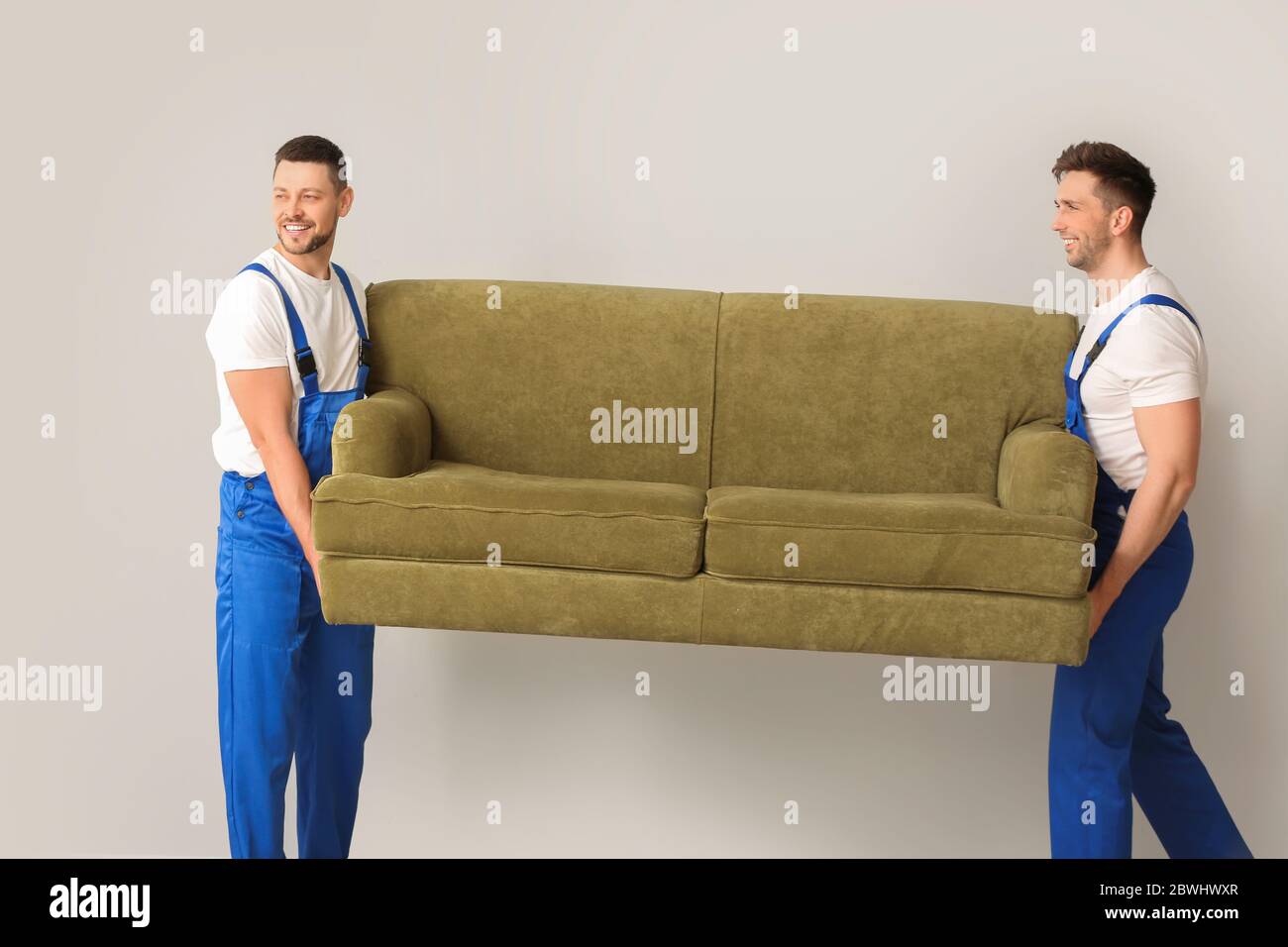 Loaders carrying furniture against grey wall Stock Photo - Alamy