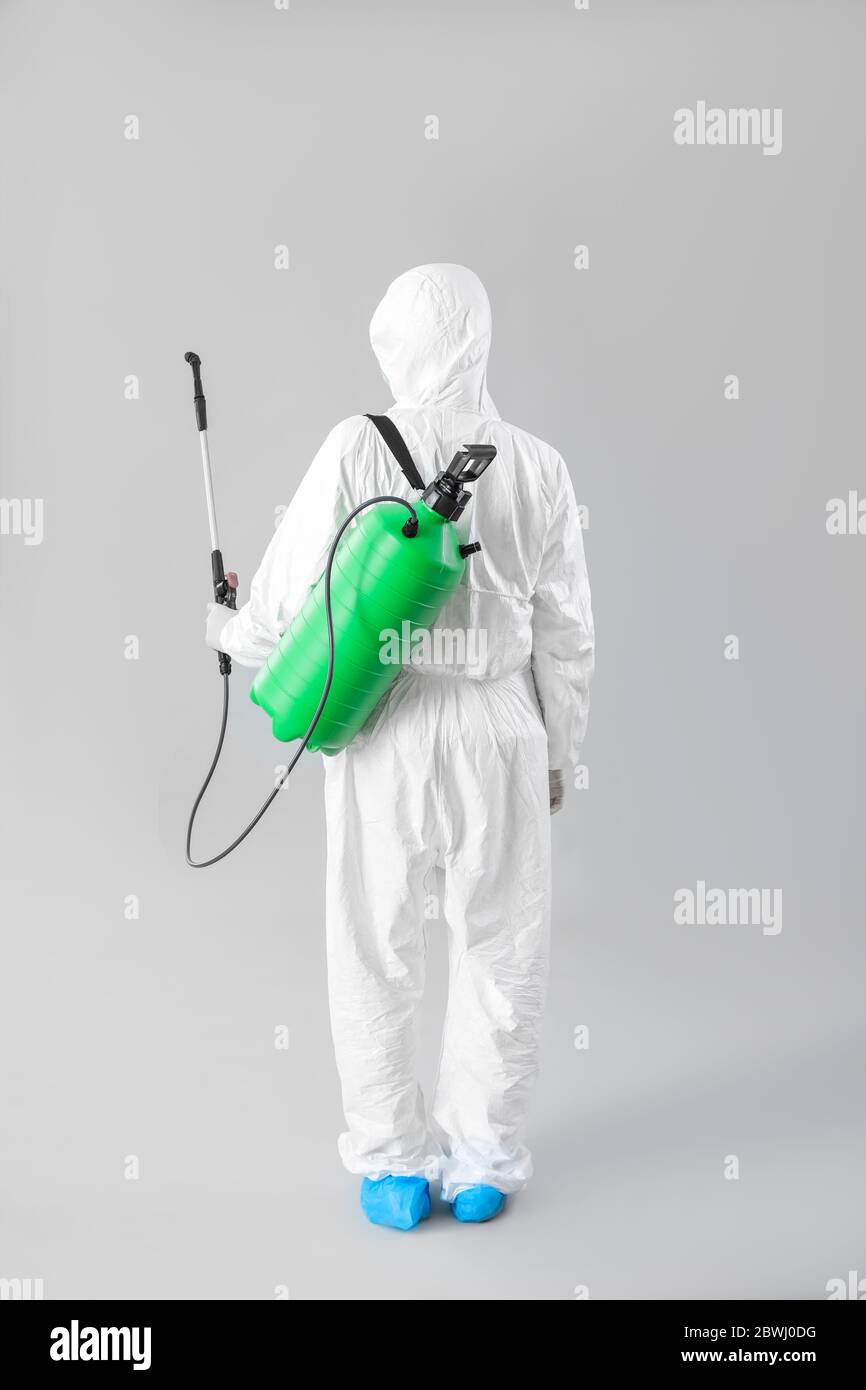 Worker in biohazard suit and with disinfectant on grey background Stock ...